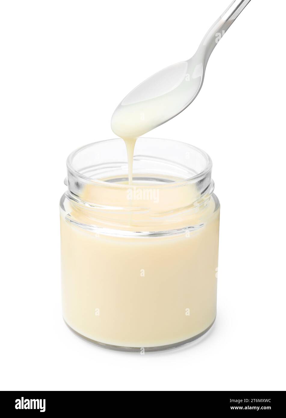 Condensed milk flowing down from spoon into jar isolated on white Stock ...