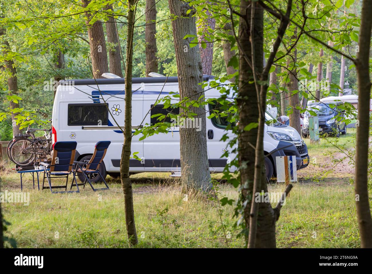 Camper bus between trees at campsite with picknick table and chairs ...