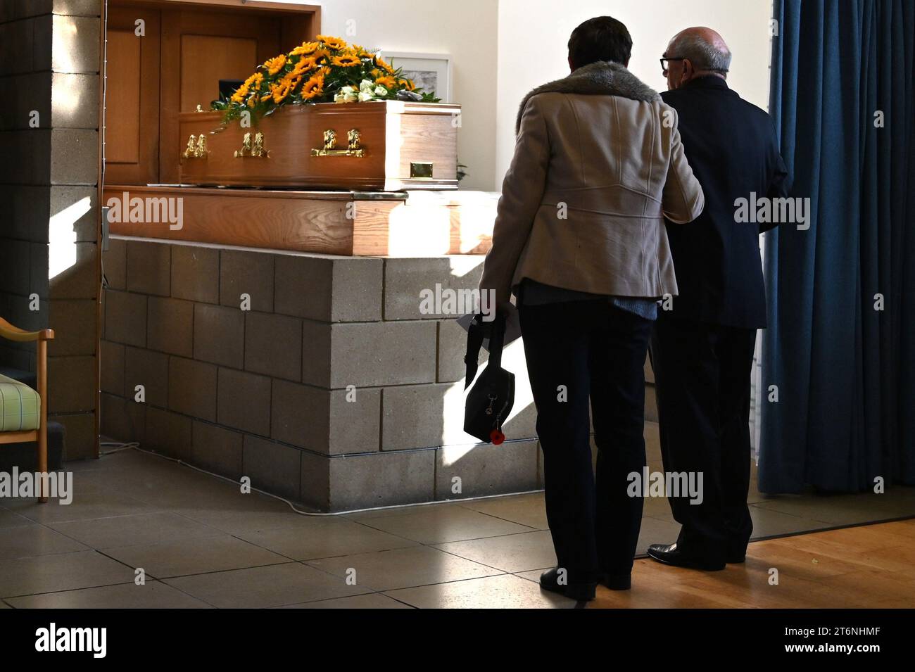 Two mourners standing in front of a coffin on a Bier at a crematorium ...