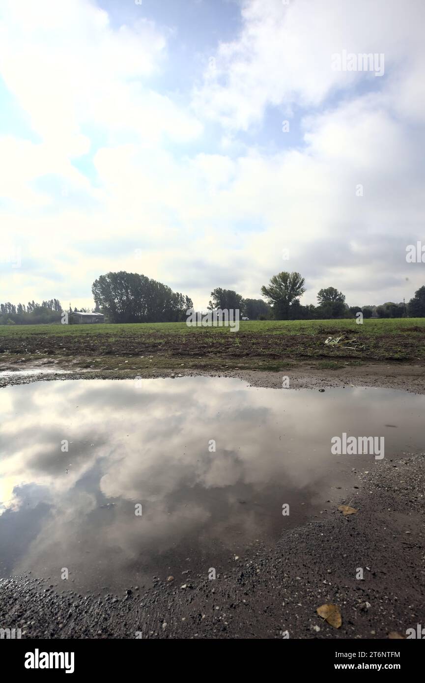 Puddle on a path next to a field with the sky casted in the water on a ...