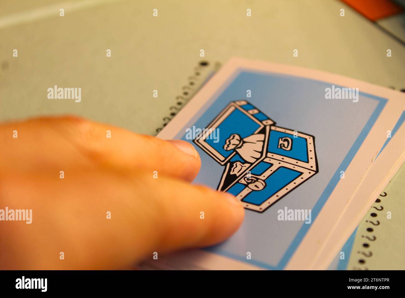 A photo of someone reaching towards a blue community chest card as part ...