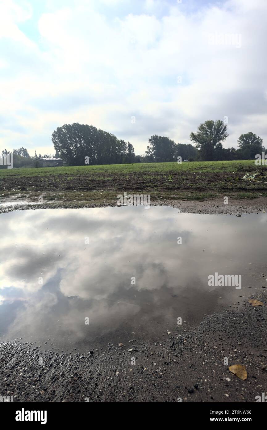 Puddle on a path next to a field with the sky casted in the water on a ...