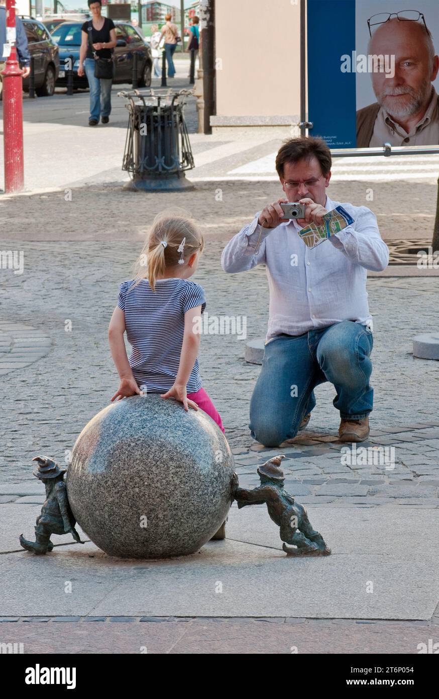 Dad taking pictures of child at sculpture of Ball-pushing and lifting ...