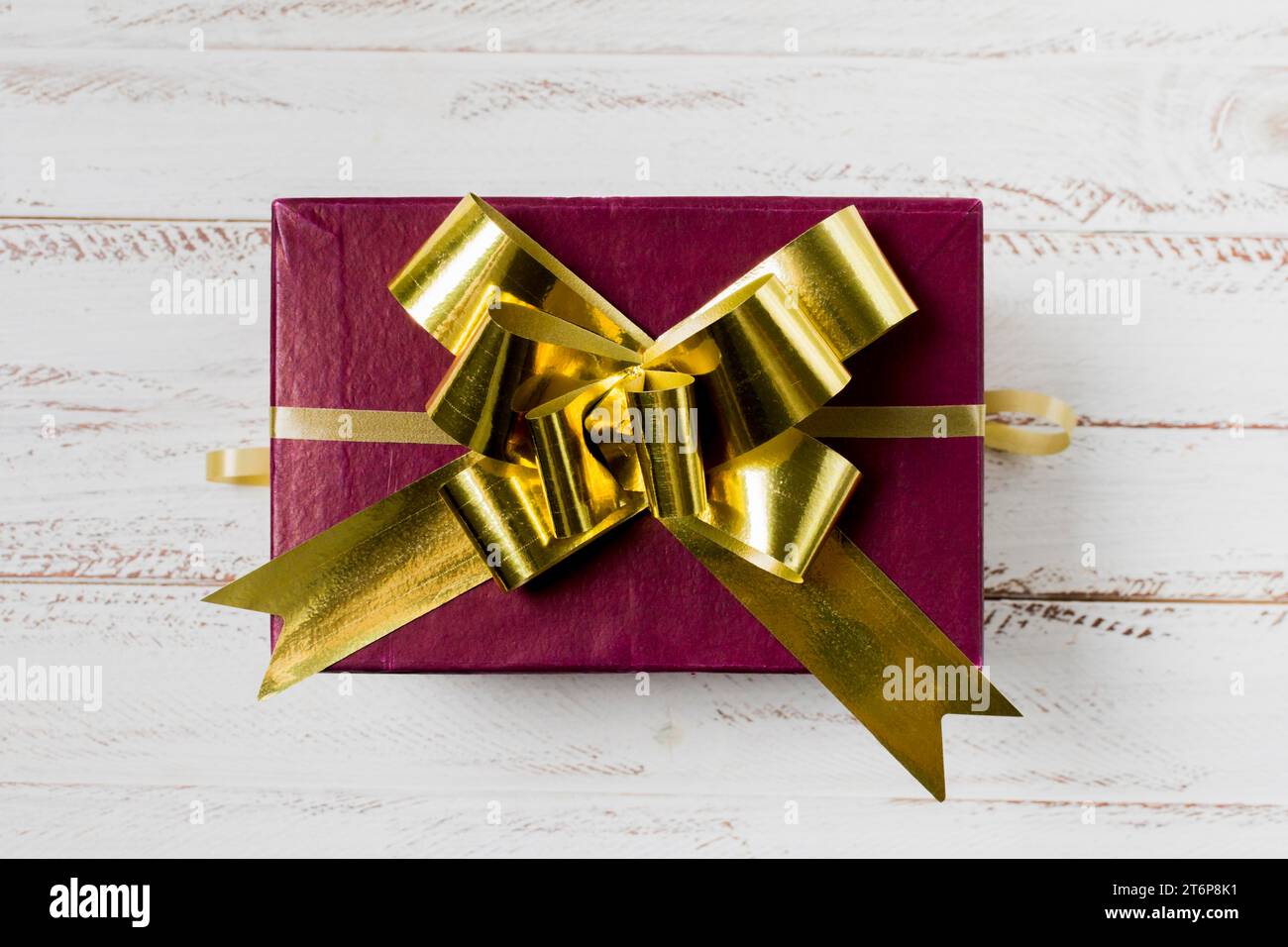 Maroon gift box with golden ribbon wooden desk Stock Photo - Alamy