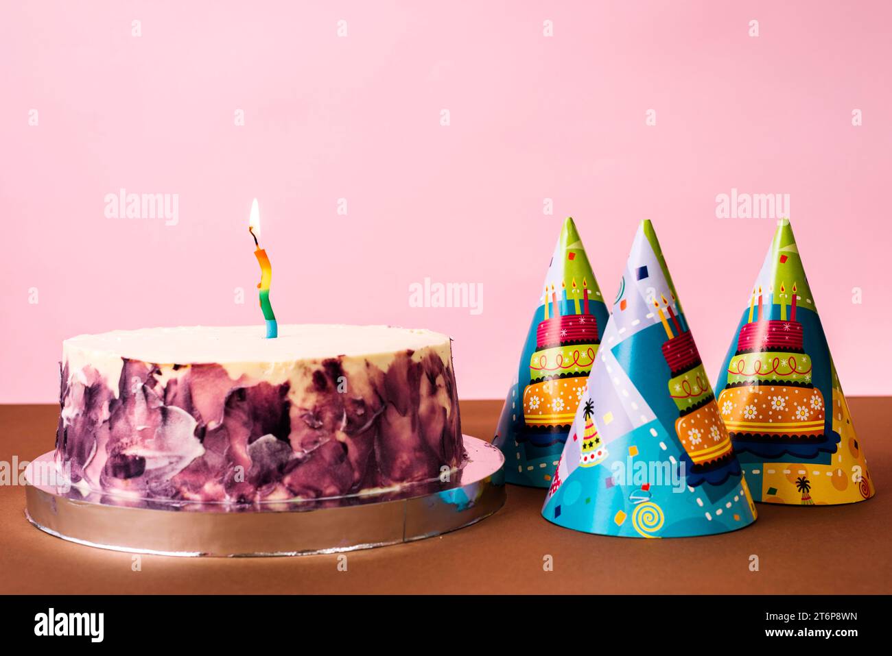 Party hats cake with lighted candle desk against pink backdrop Stock ...