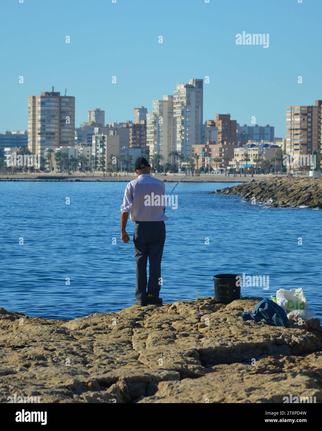 A vertical rear view of a male fishing on a rocky outcropping in ...
