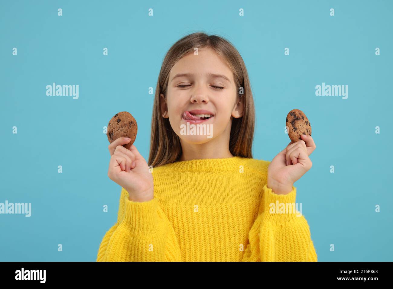 Cute girl with chocolate chip cookies showing tongue on light blue ...