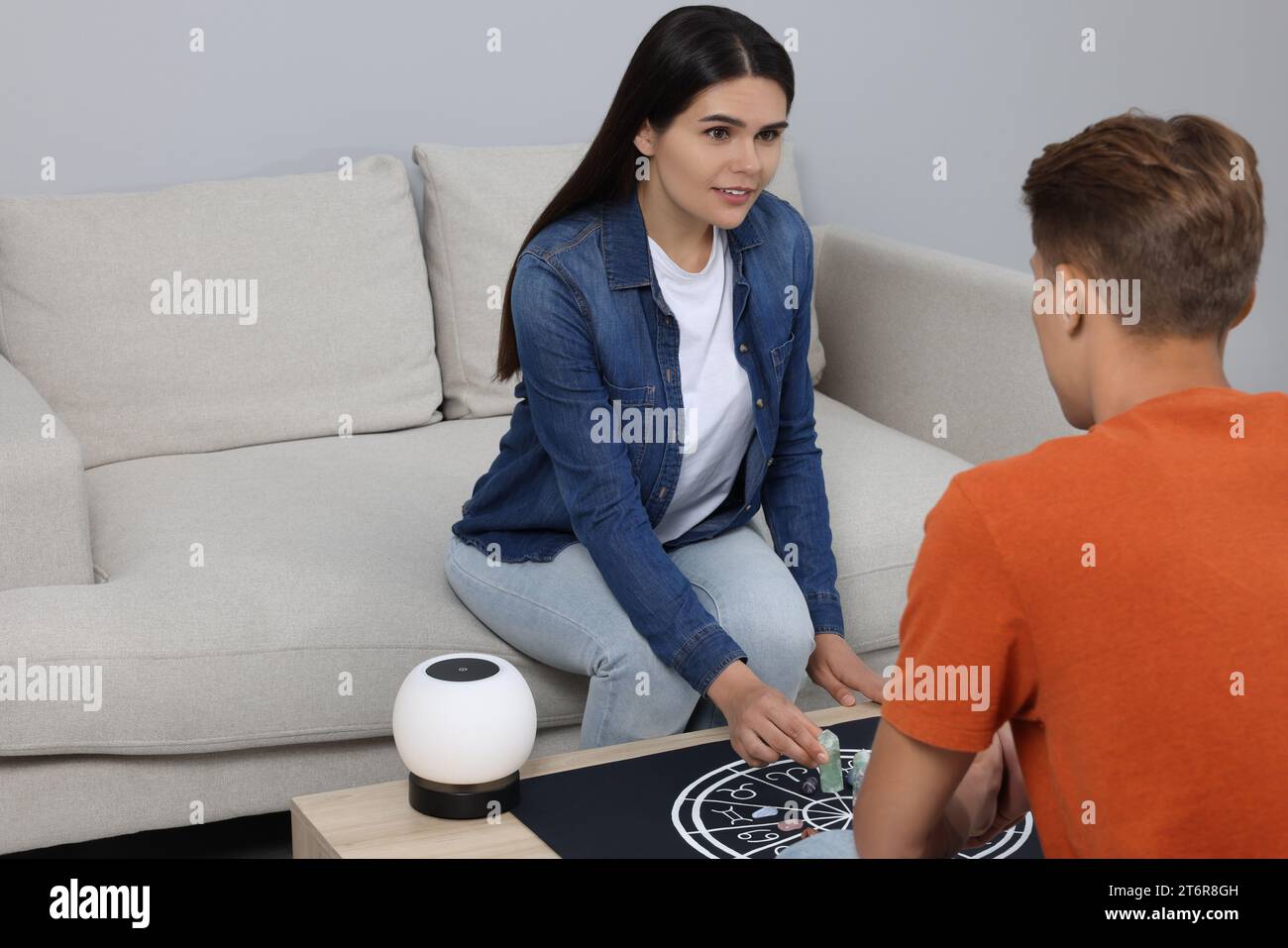 Astrologer predicting client's future with zodiac wheel, stones and crystals at wooden table ...
