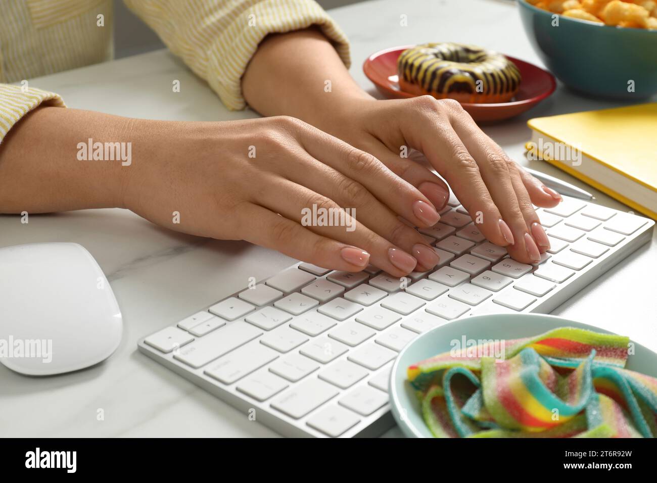 Bad eating habits. Woman working on computer at white marble table with ...