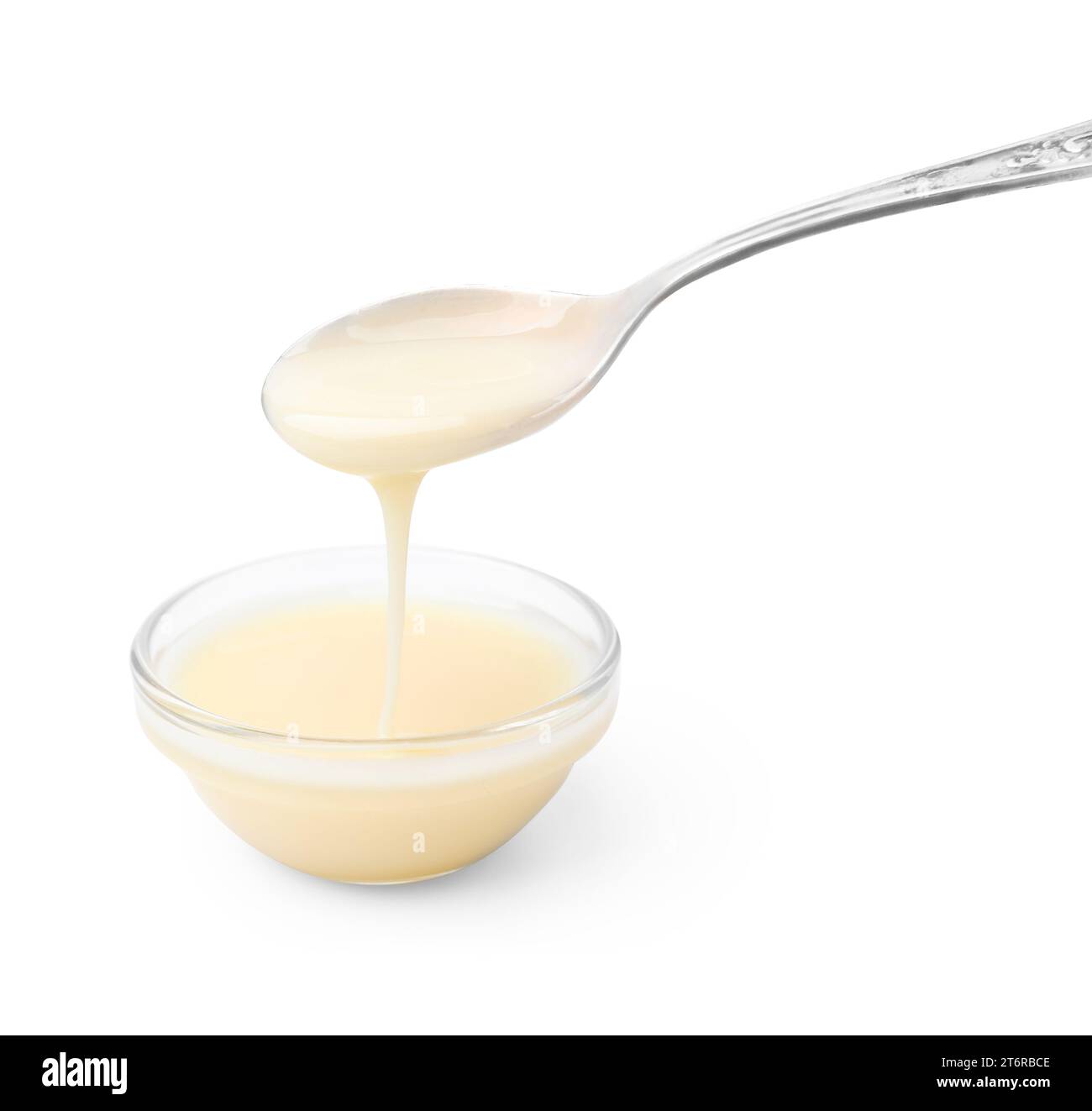 Condensed milk flowing down from spoon into bowl isolated on white ...