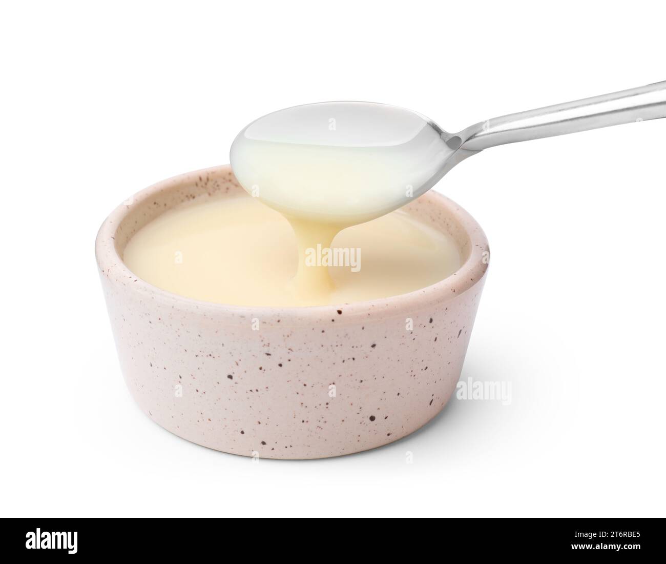 Condensed milk flowing down from spoon into bowl isolated on white ...