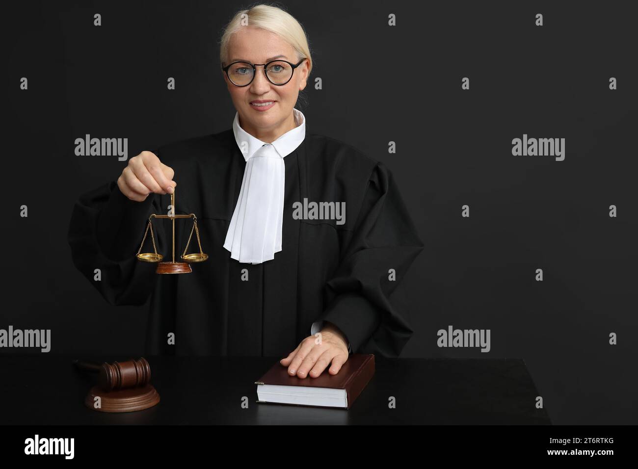 Mature female judge with scales of justice and book at table on black ...