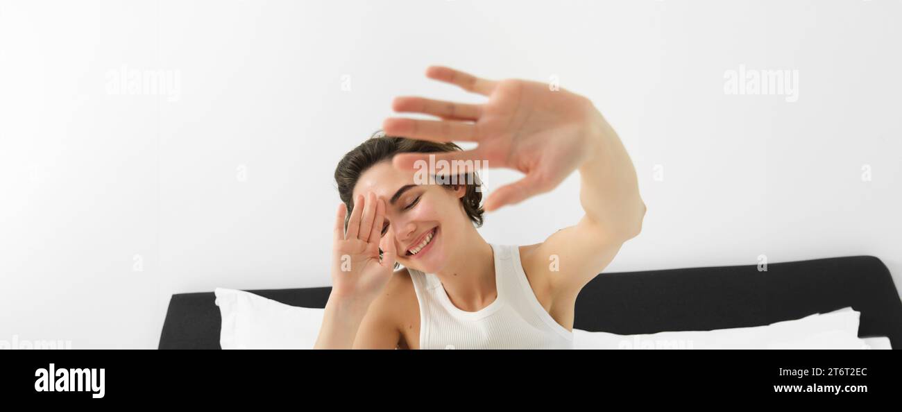 Portrait of sleepy, happy young woman, wakes up in her bed, stretching ...
