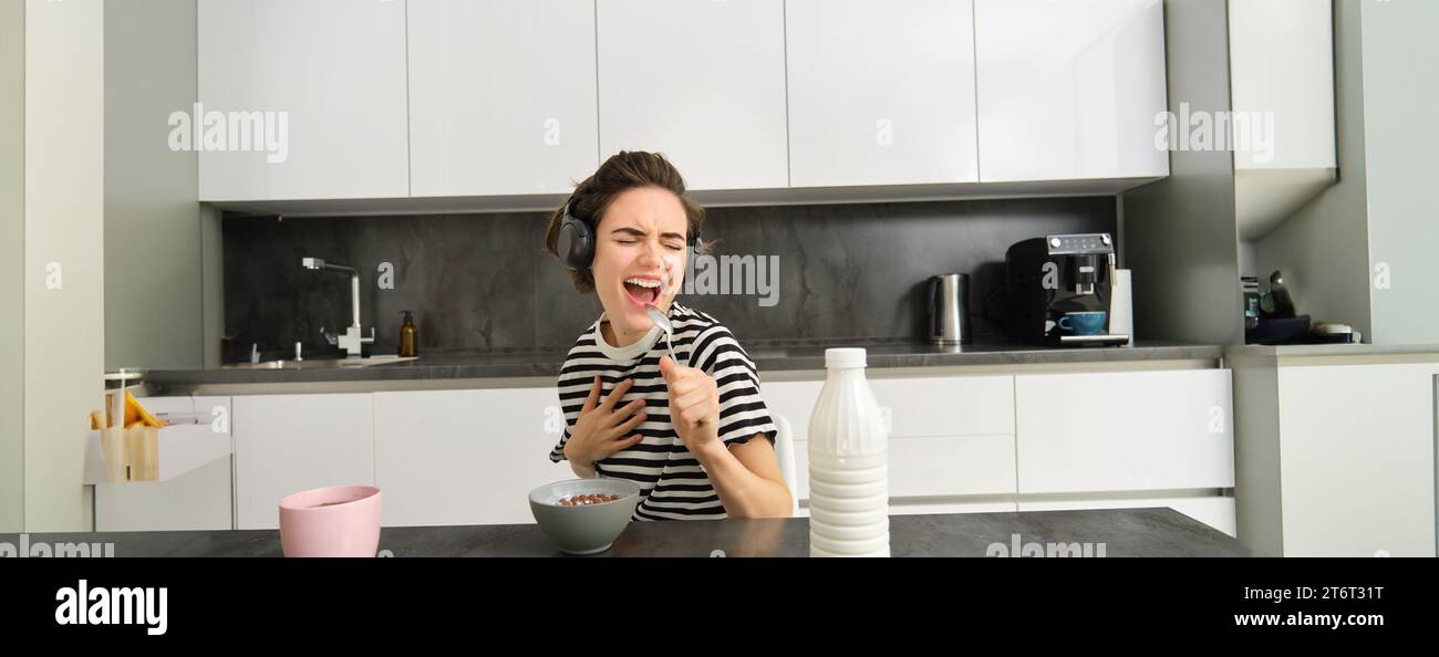 Happy and emotional young woman, singing while eating breakfast, having ...