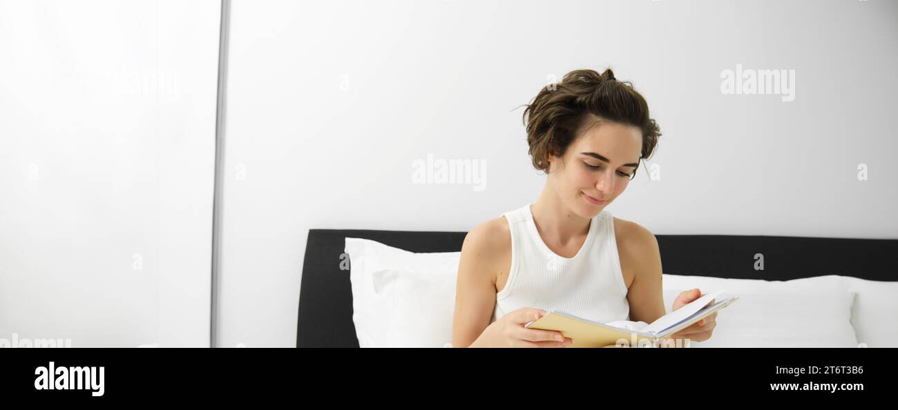 Portrait of woman in bed, holding journal, reading notebook and smiling ...