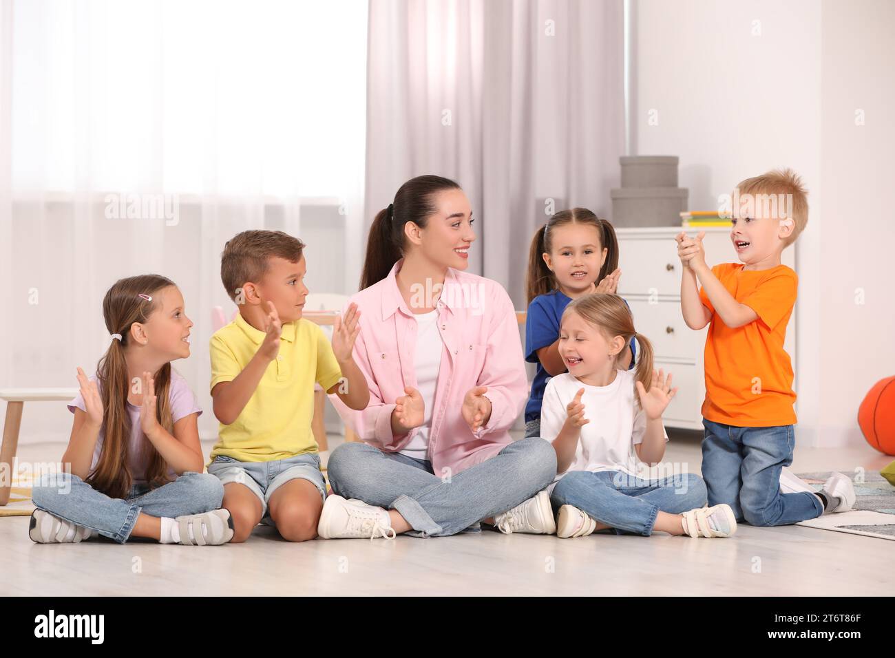 Nursery teacher and group of cute little children spending time ...