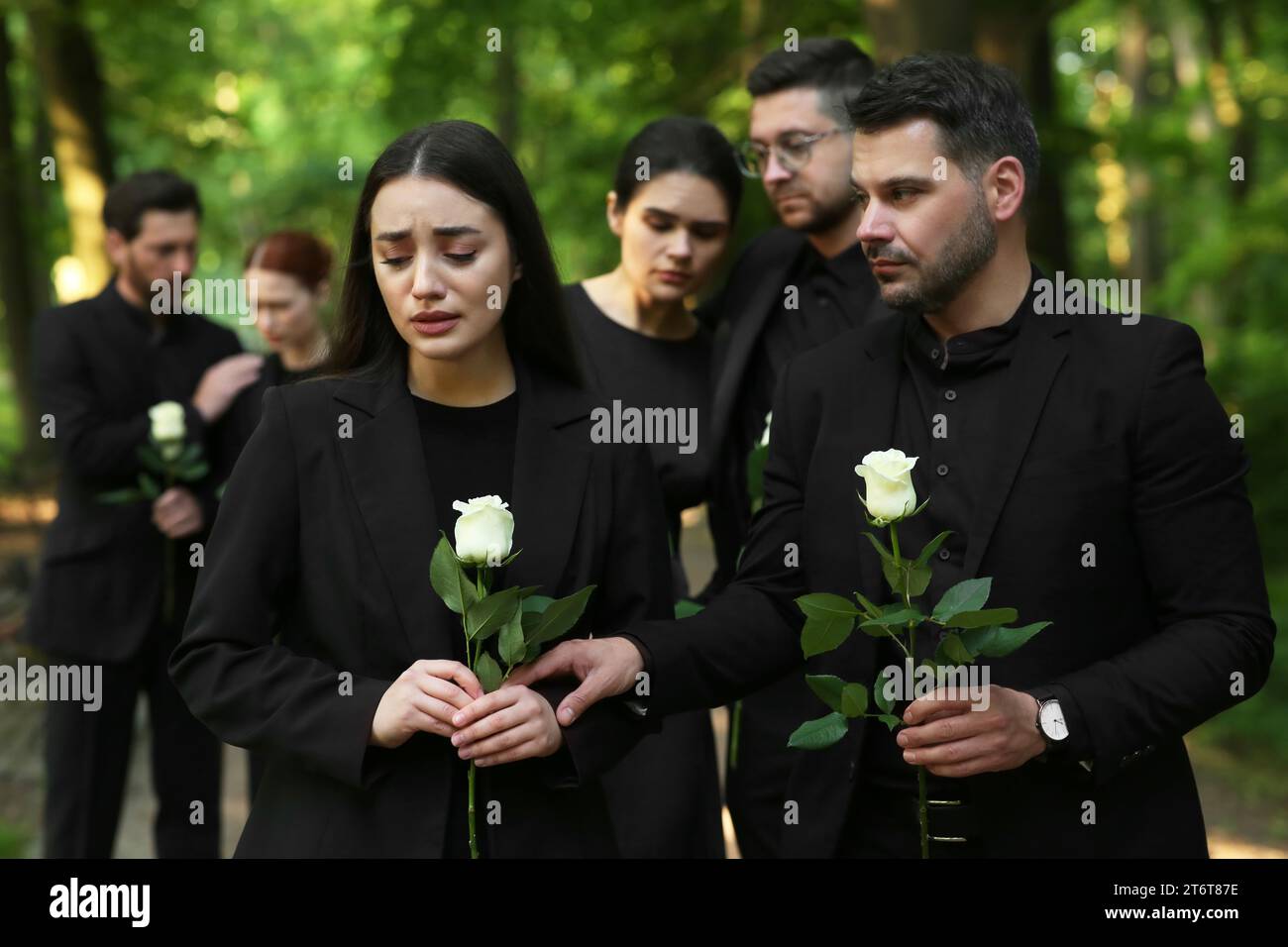 Funeral ceremony. Sad people with white rose flowers mourning outdoors ...