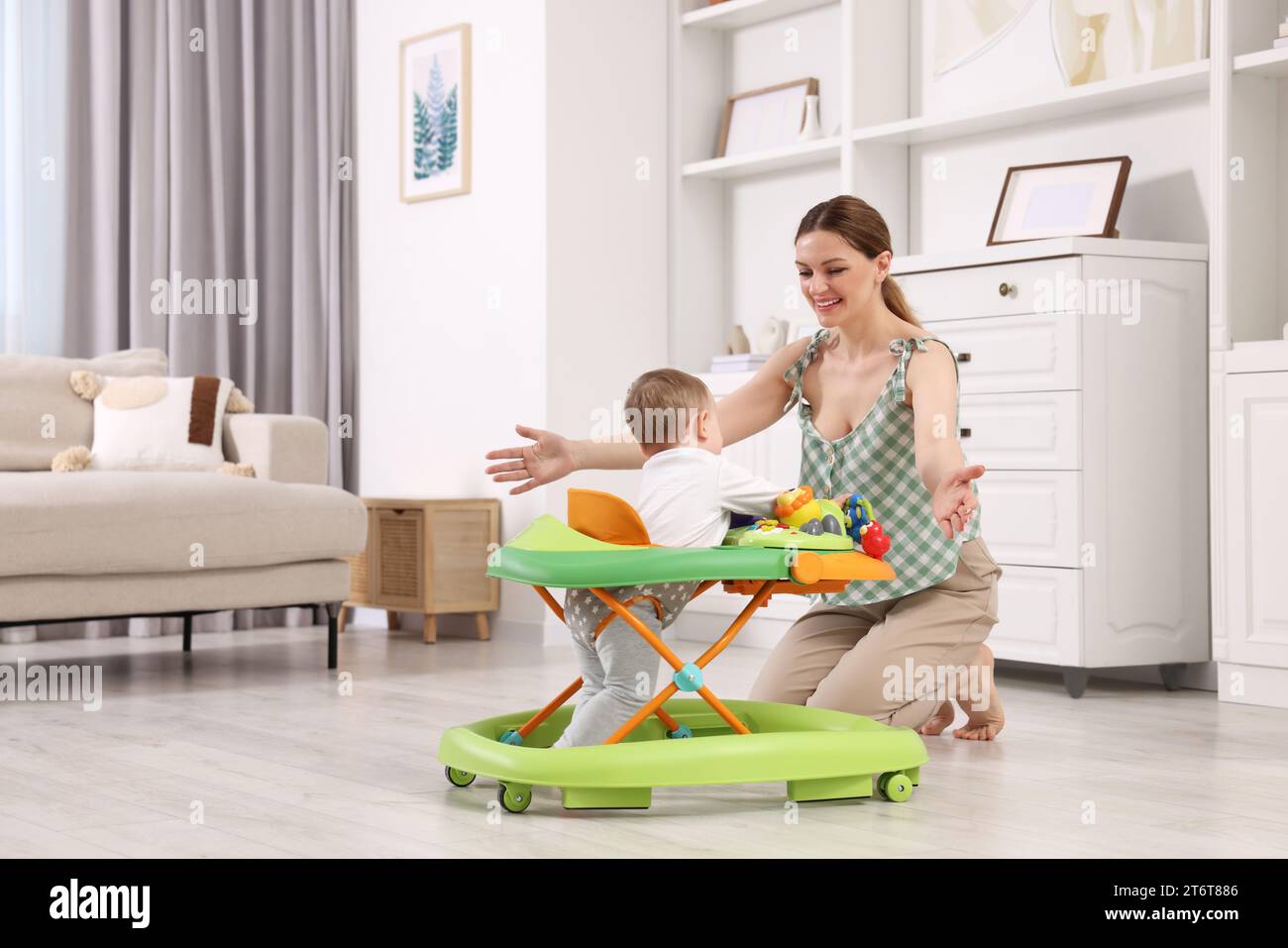 Little boy in baby walker hurrying to mother at home. Woman calling ...