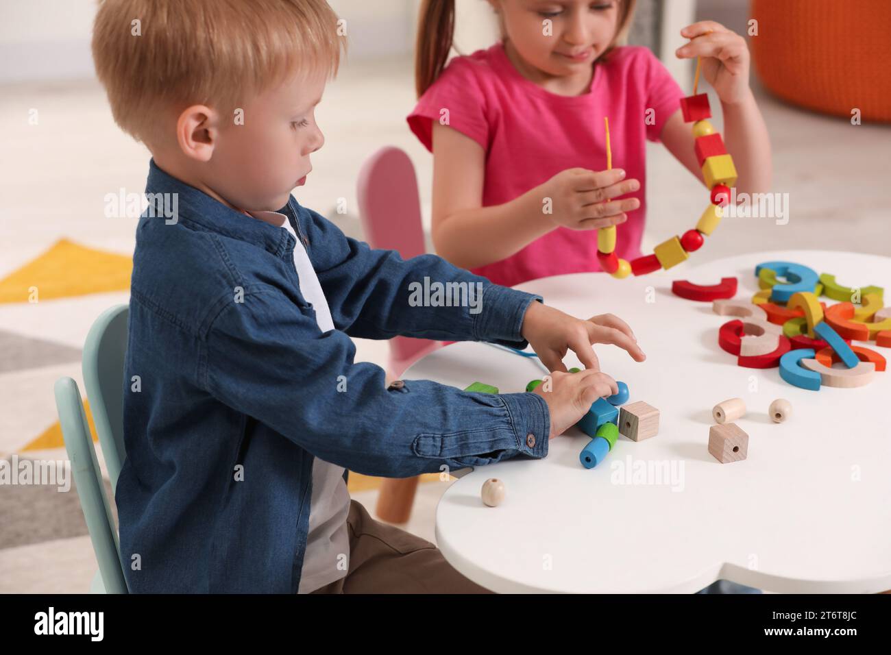 Little children playing with wooden pieces and string for threading ...