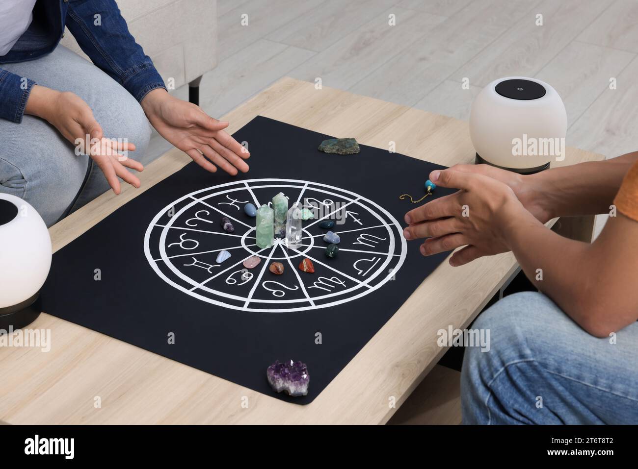 Astrologer predicting client's future with zodiac wheel, stones and crystals at wooden table ...