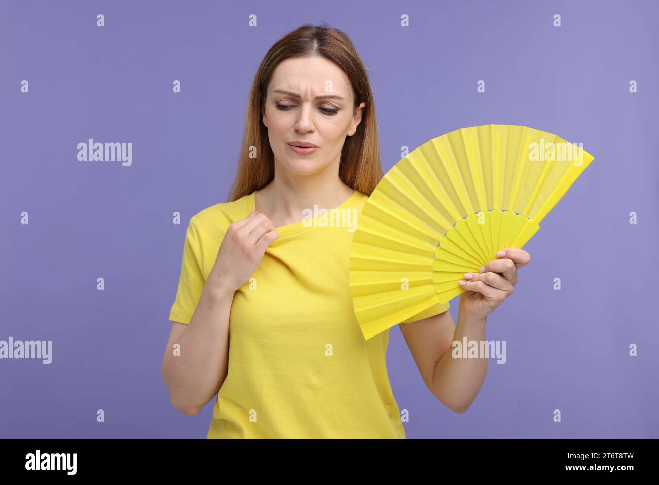 Beautiful woman waving yellow hand fan to cool herself on violet ...