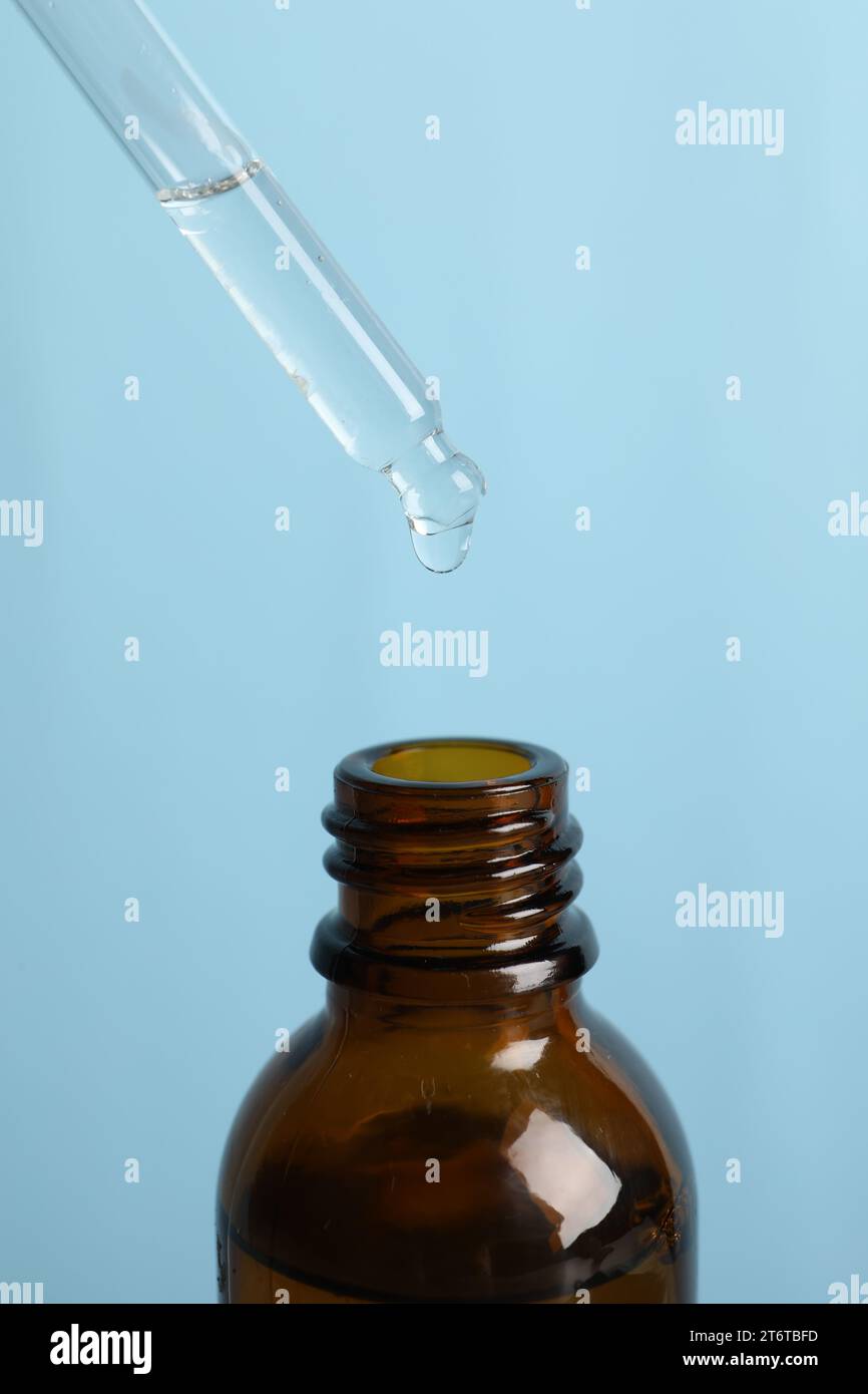 Dripping cosmetic serum from pipette into bottle on light blue ...