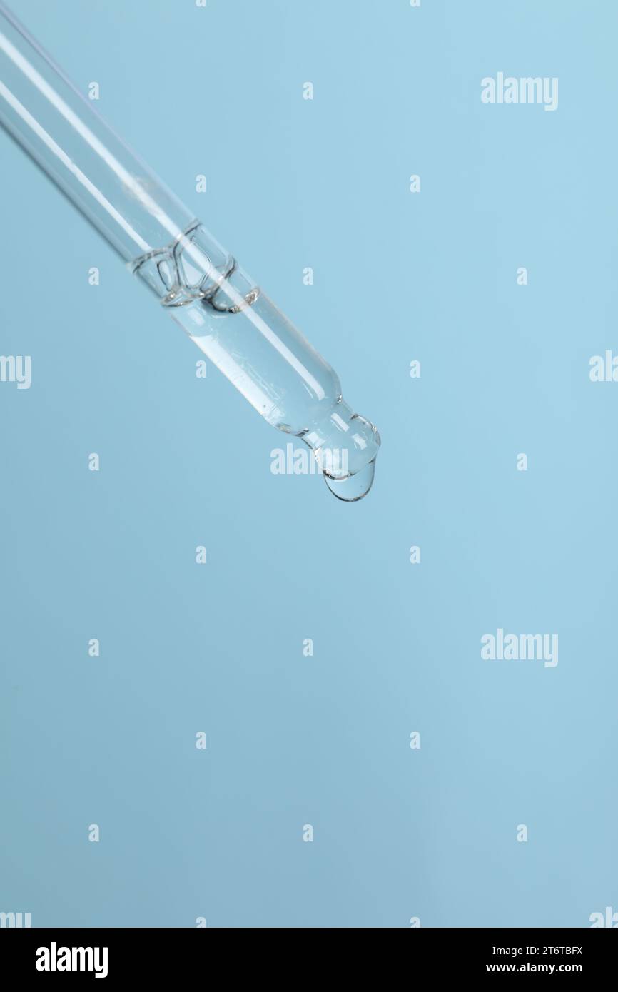 Dripping cosmetic serum from pipette on light blue background Stock ...
