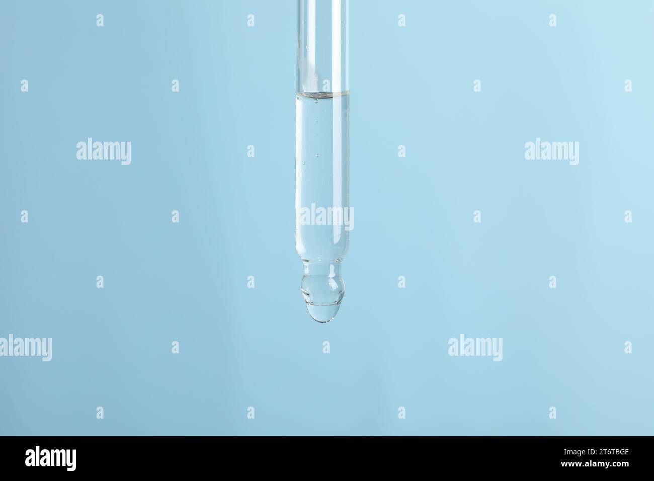 Dripping cosmetic serum from pipette on light blue background Stock ...