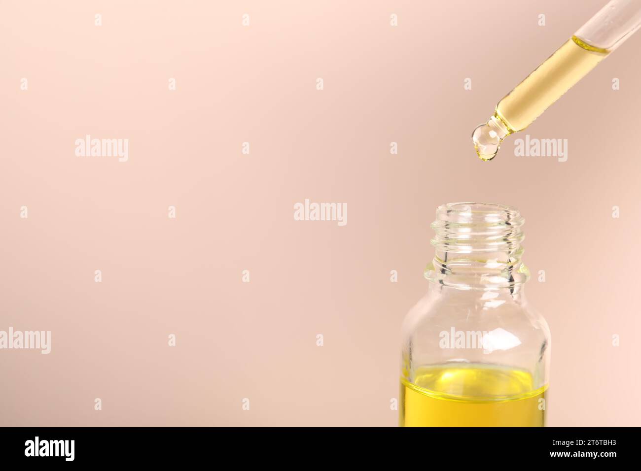 Dripping cosmetic serum from pipette into bottle on beige background ...