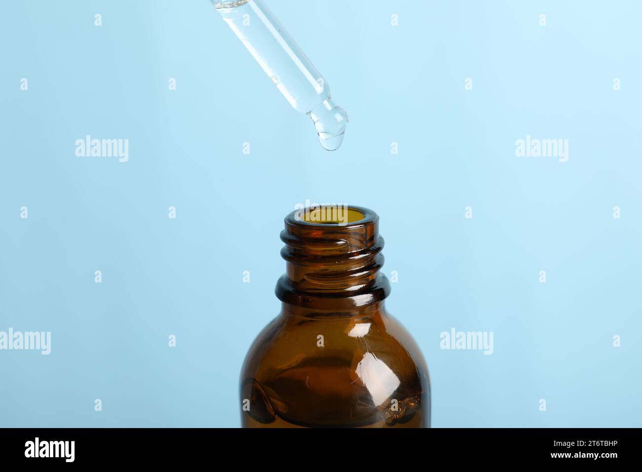 Dripping cosmetic serum from pipette into bottle on light blue ...