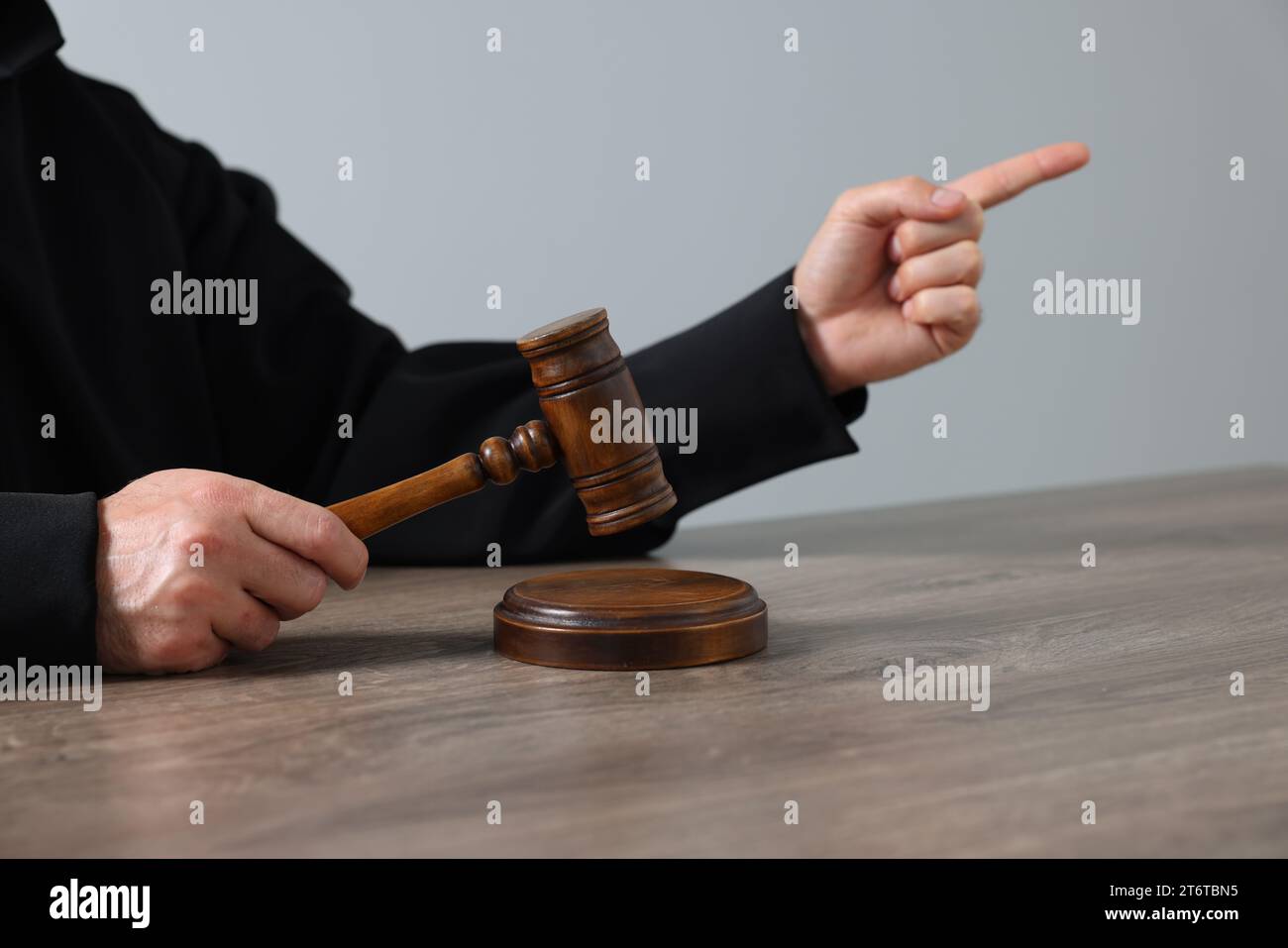 Judge with gavel sitting at wooden table against light grey background ...