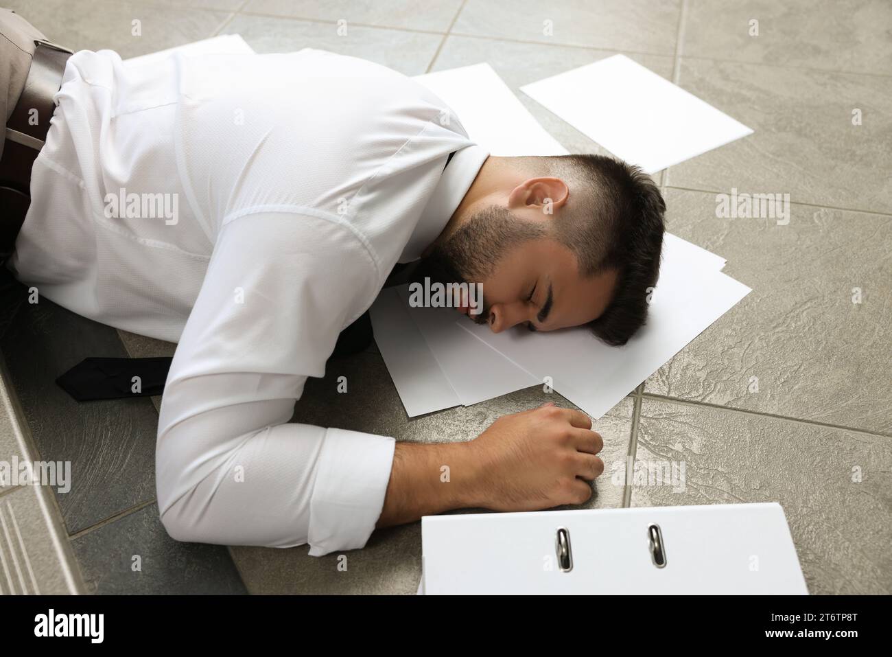 Unconscious man with scattered folder and papers lying on floor after ...