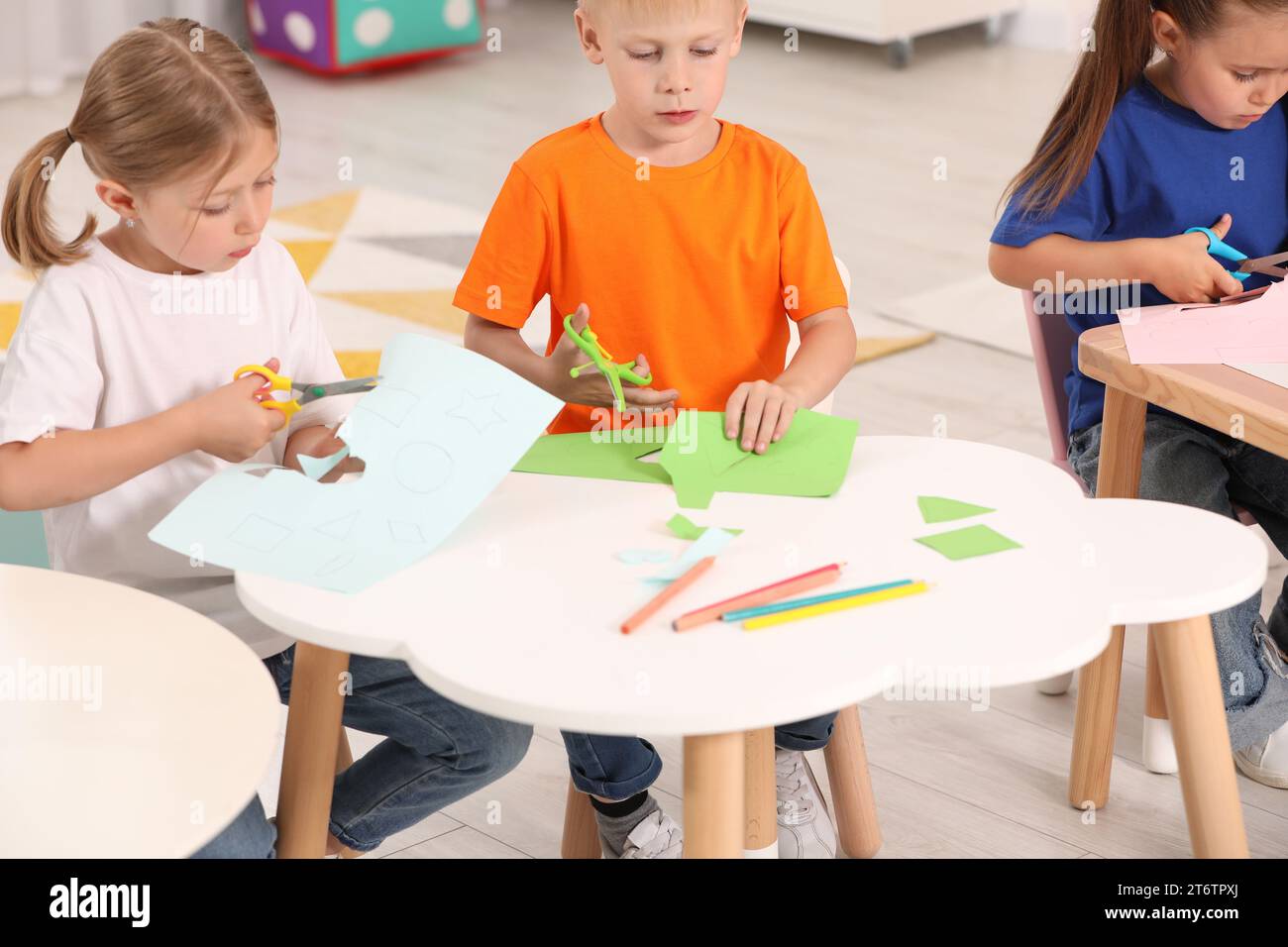 Cute little children cutting color paper with scissors at desks in ...