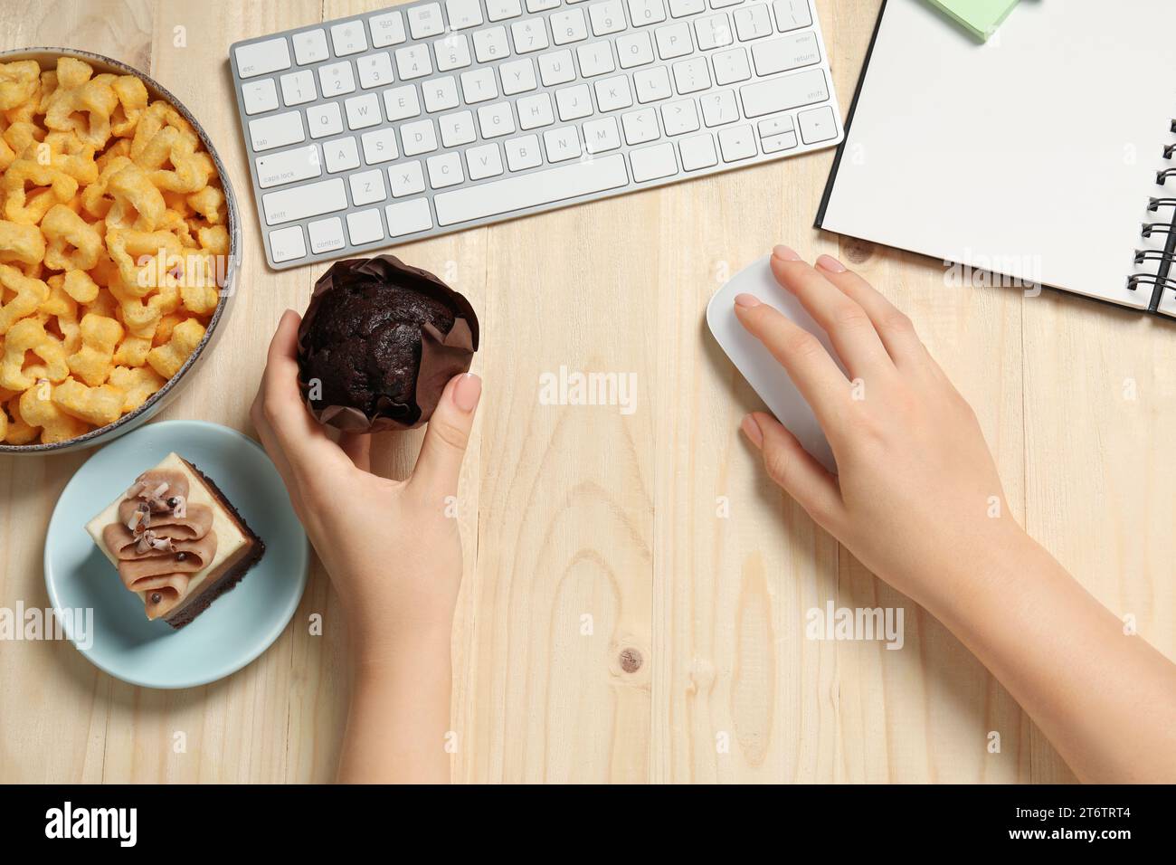 Bad habits. Woman eating muffin while working on computer at wooden ...