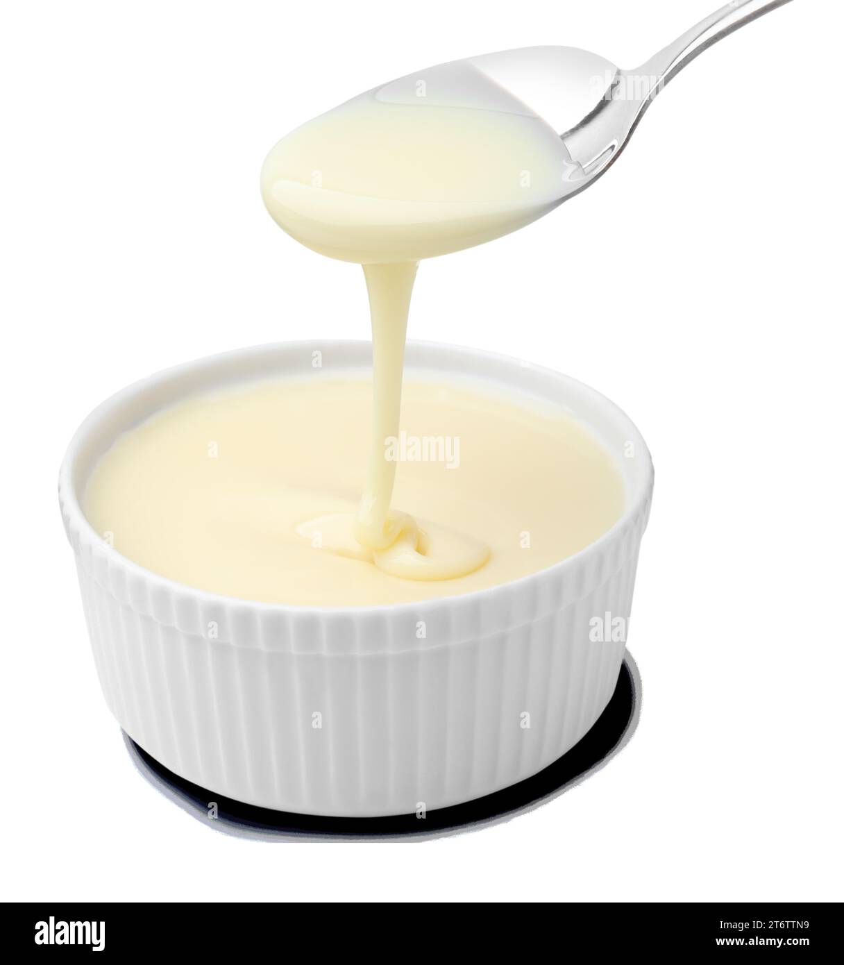 Condensed milk flowing down from spoon into bowl isolated on white ...