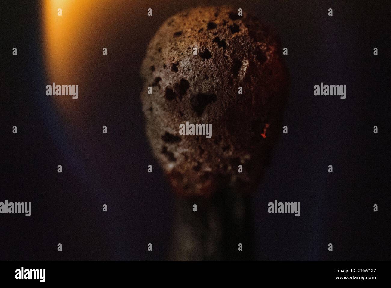 An image of a lit matchstick against a dark blue background, emitting a ...