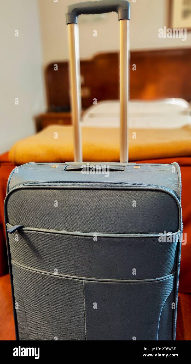 detail of a blue suitcase arriving at a hotel room with the bed in the ...