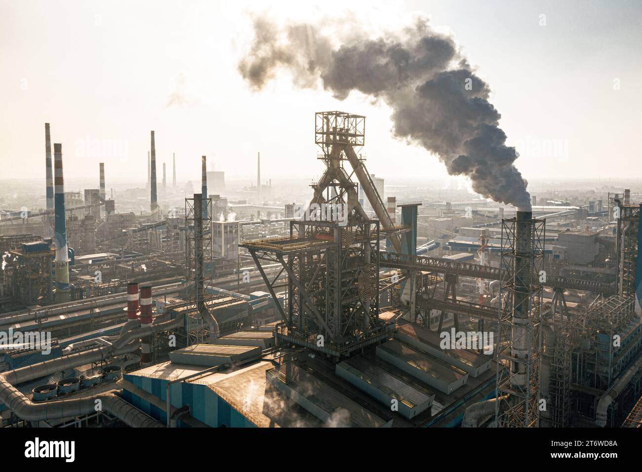 This image is of a large industrial factory with white smoke billowing ...