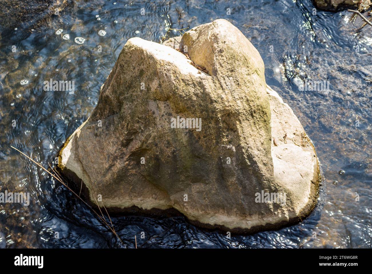 A large light-colored boulder lying in the water in a stream Stock ...