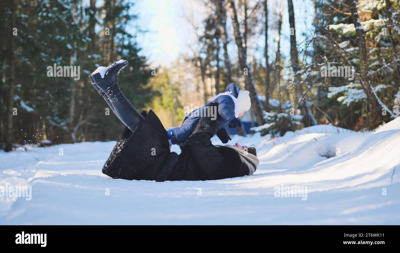 A mother and her child playing in the winter woods, falling in the snow ...