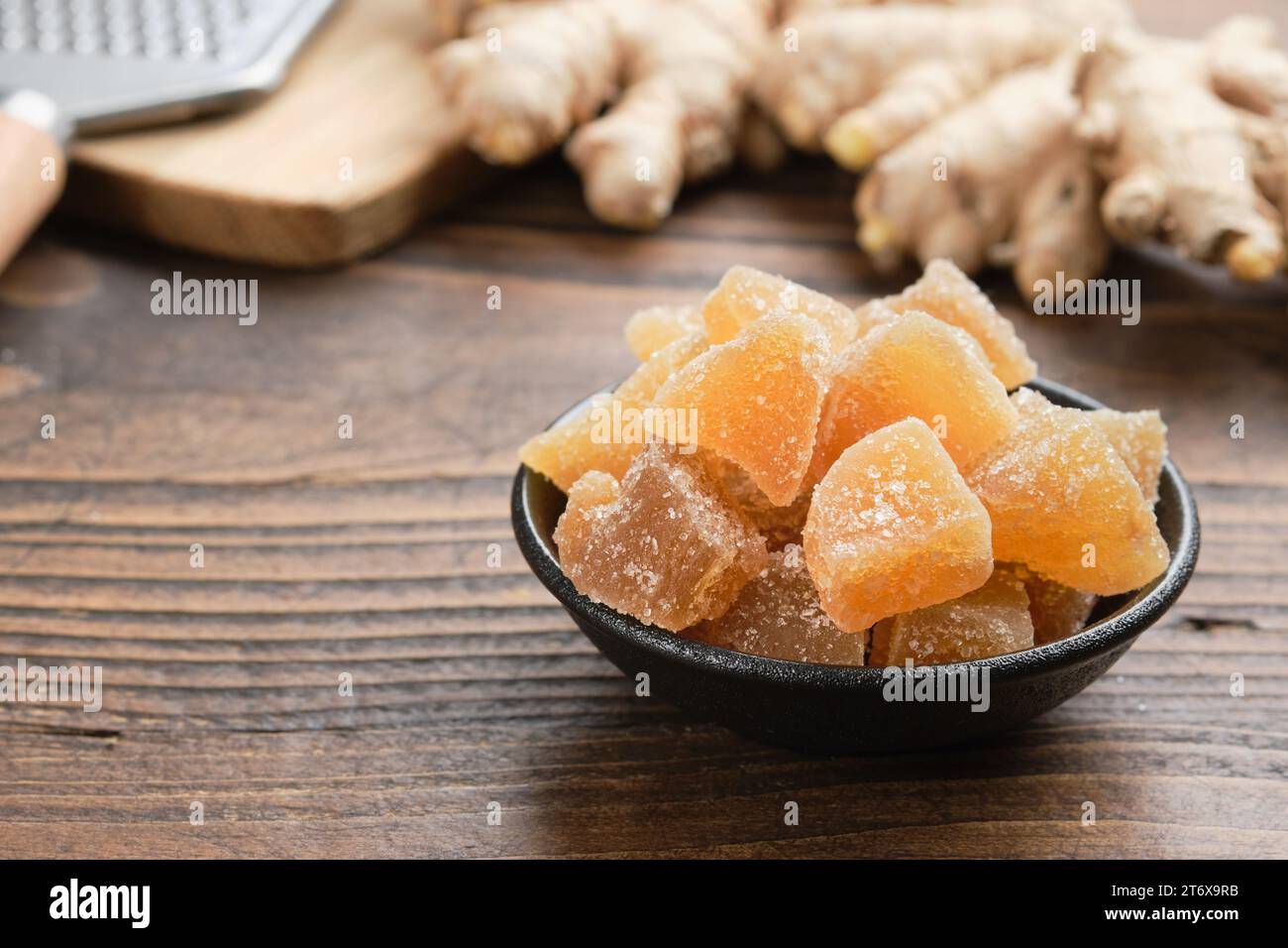 Bowl of candied ginger pieces and ginger roots on wooden kitchen table ...
