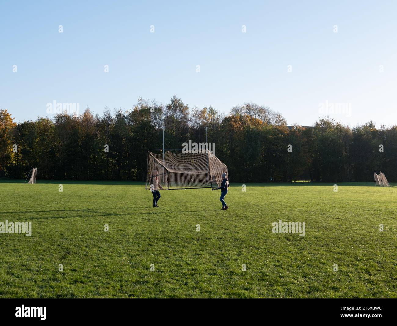 Two people carrying a sports goal across a pitch Stock Photo - Alamy
