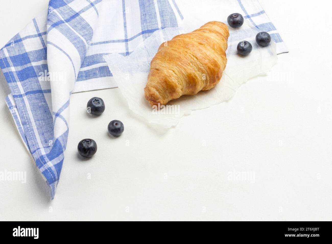 Croissant on white and blue checkered napkin. Blueberries on table. Top ...