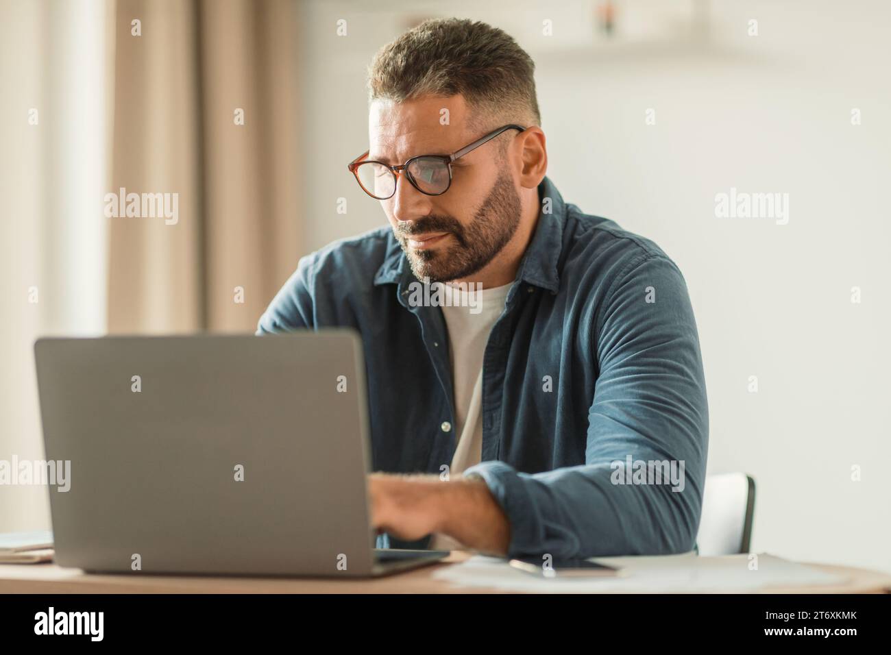 Serious middle aged man types focused on his laptop indoor Stock Photo ...