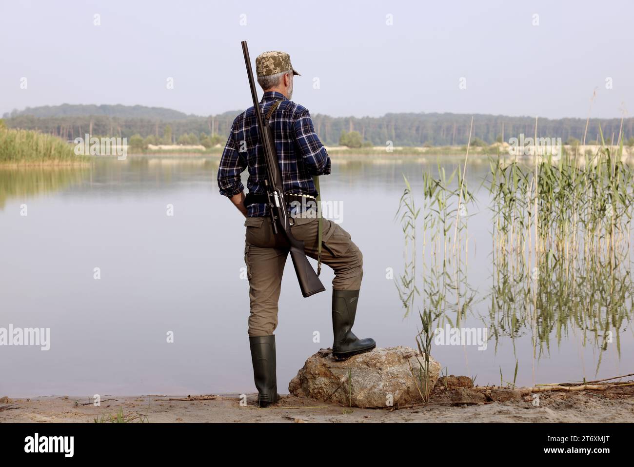 Man with hunting rifle near lake outdoors, back view Stock Photo - Alamy