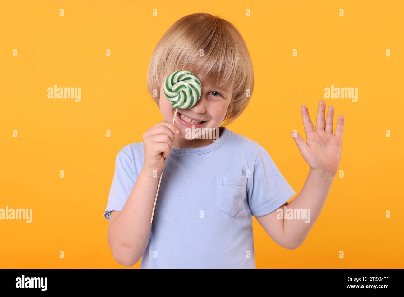 Happy little boy covering his eye with bright lollipop swirl on orange ...