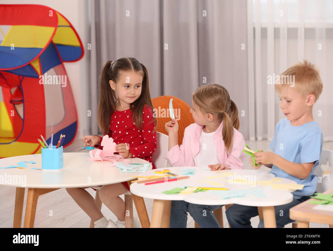 Group of cute little children making toys from color paper at desks in ...