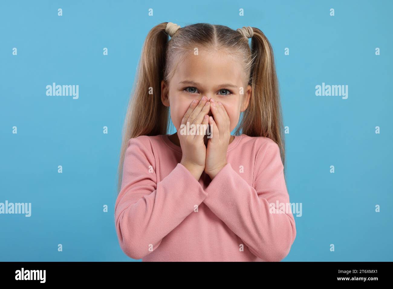 Embarrassed little girl covering her mouth with hands on light blue ...