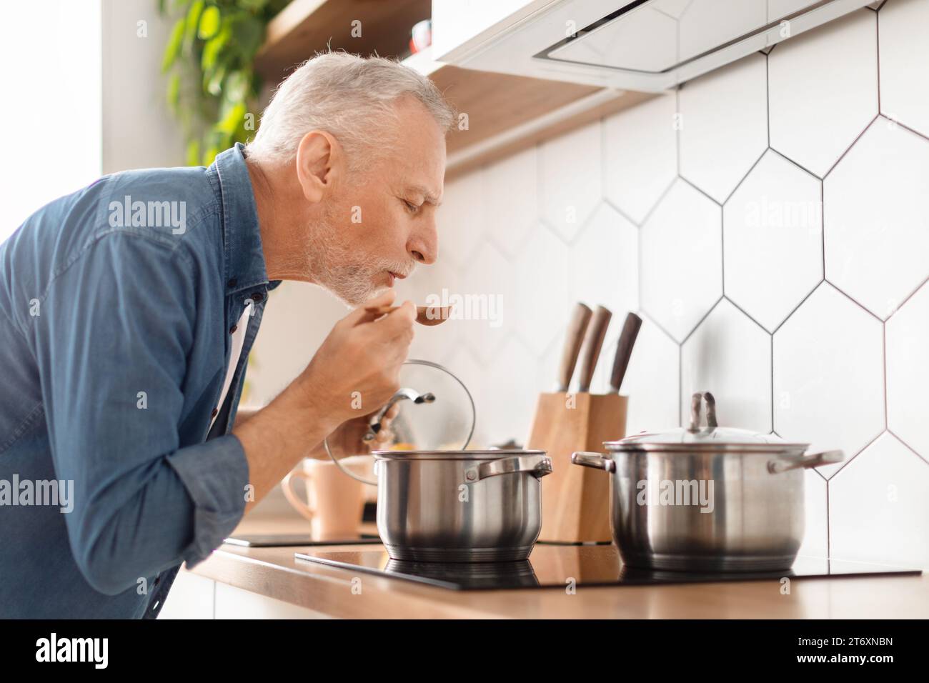 Senior man tasting food while cooking on stove in kitchen Stock Photo ...
