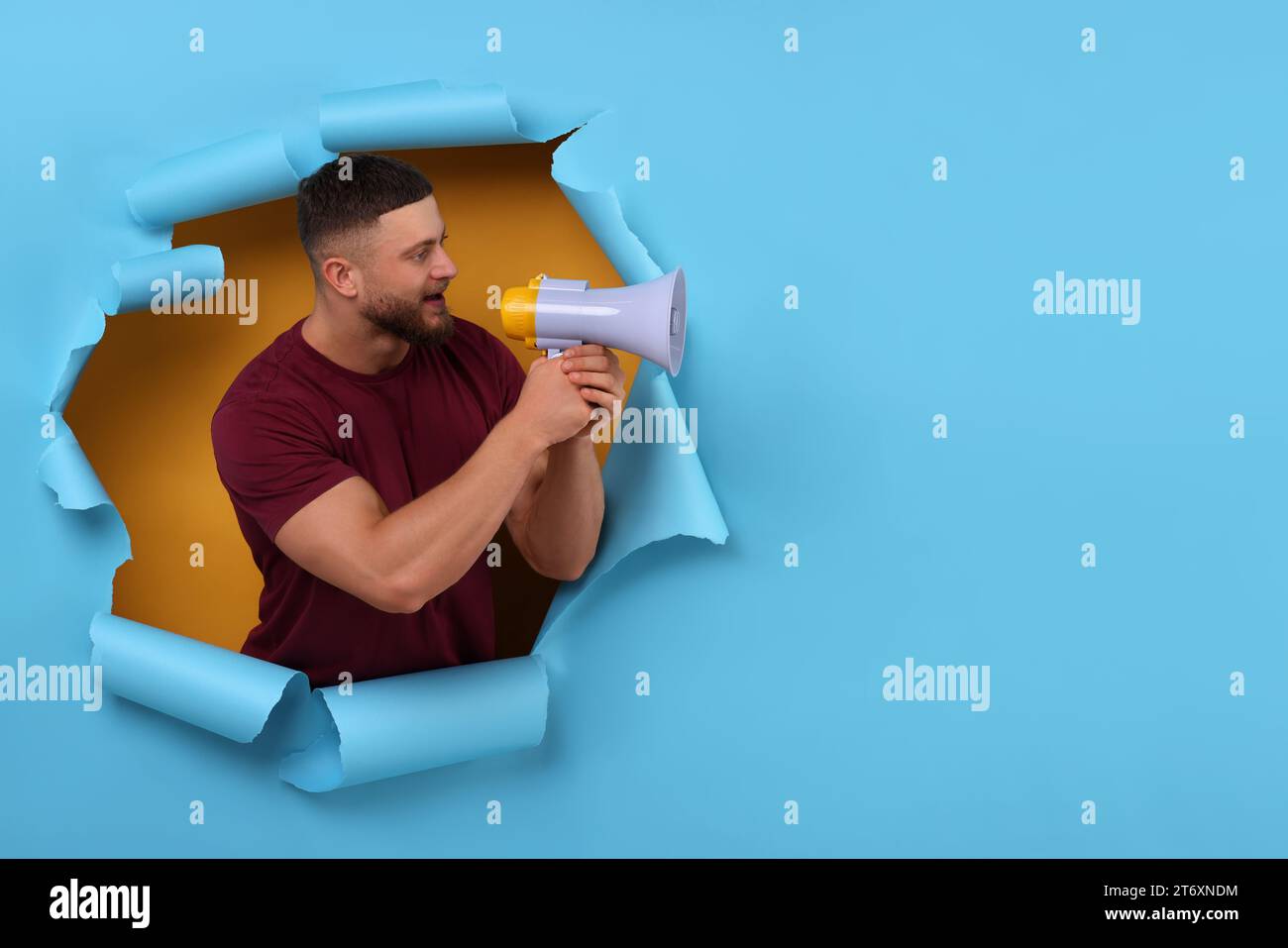 Special promotion. Young man with megaphone shouting through hole in ...